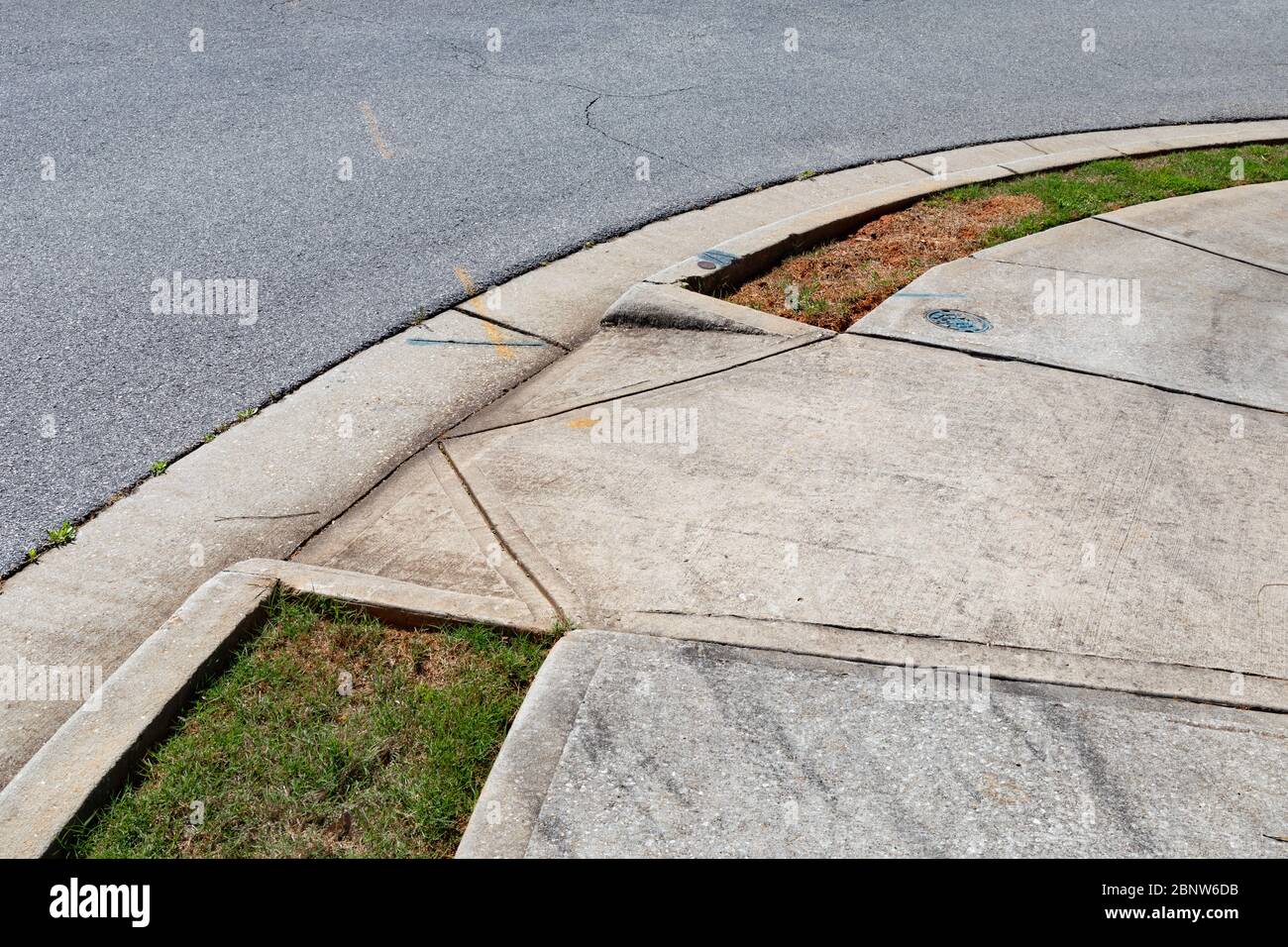 Asphalt street and concrete sidewalk with graded ramp between, green ...