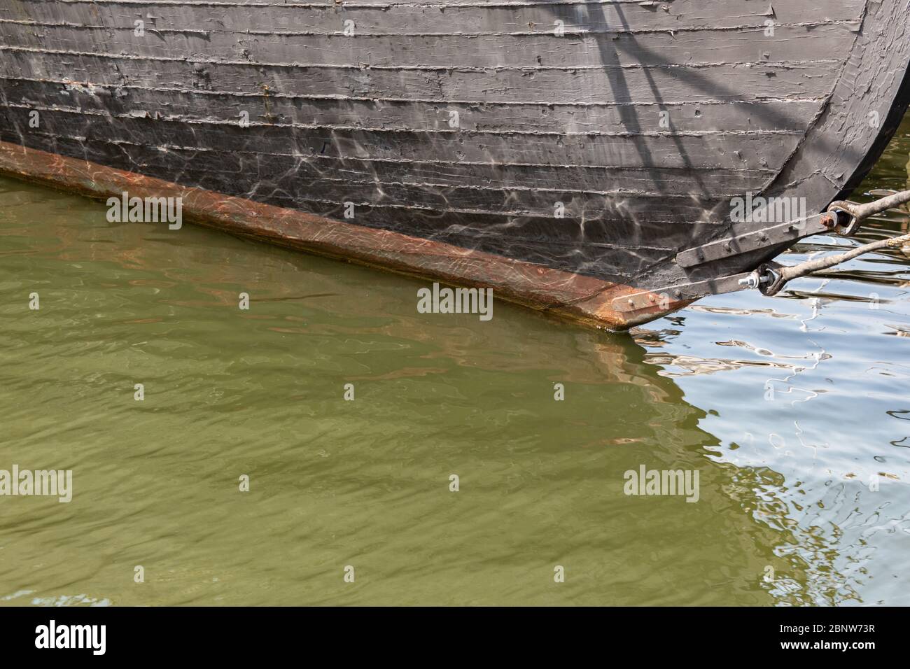 Detail of the black painted hull of an old wooden ship, green sea water ...