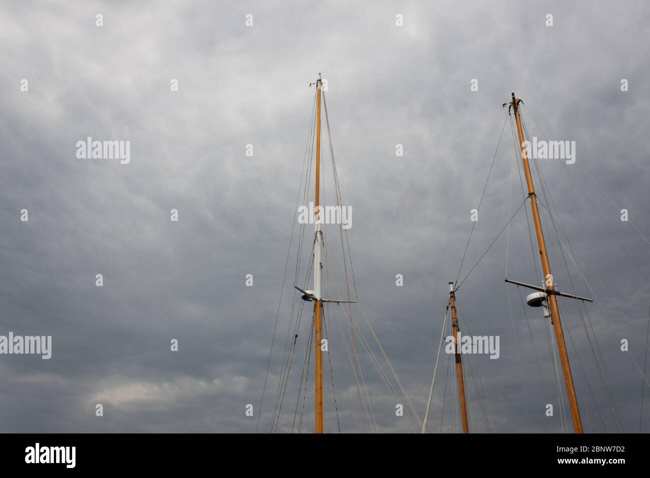 Trio of ship masts, rigging but no sails, against threatening skies ...