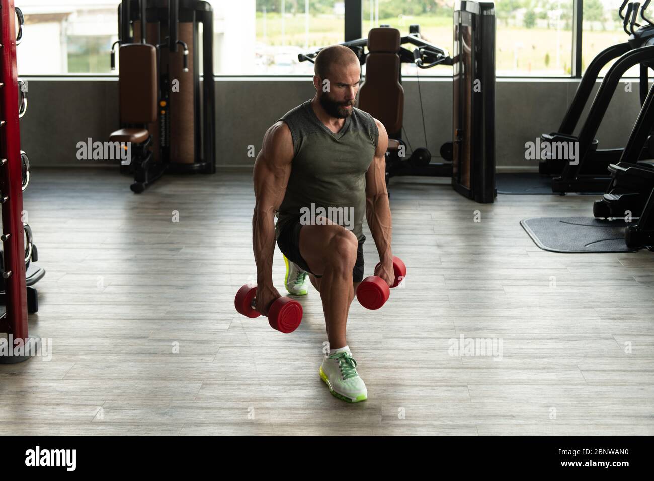 Strong Man In The Gym Exercising Legs With Dumbbells - Muscular ...