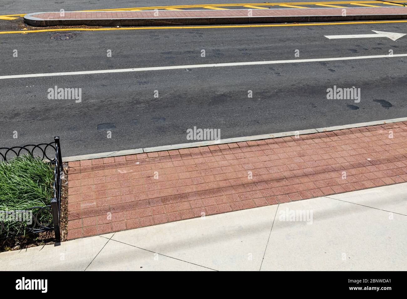 Urban asphalt street with traffic island, curb with red brick border ...