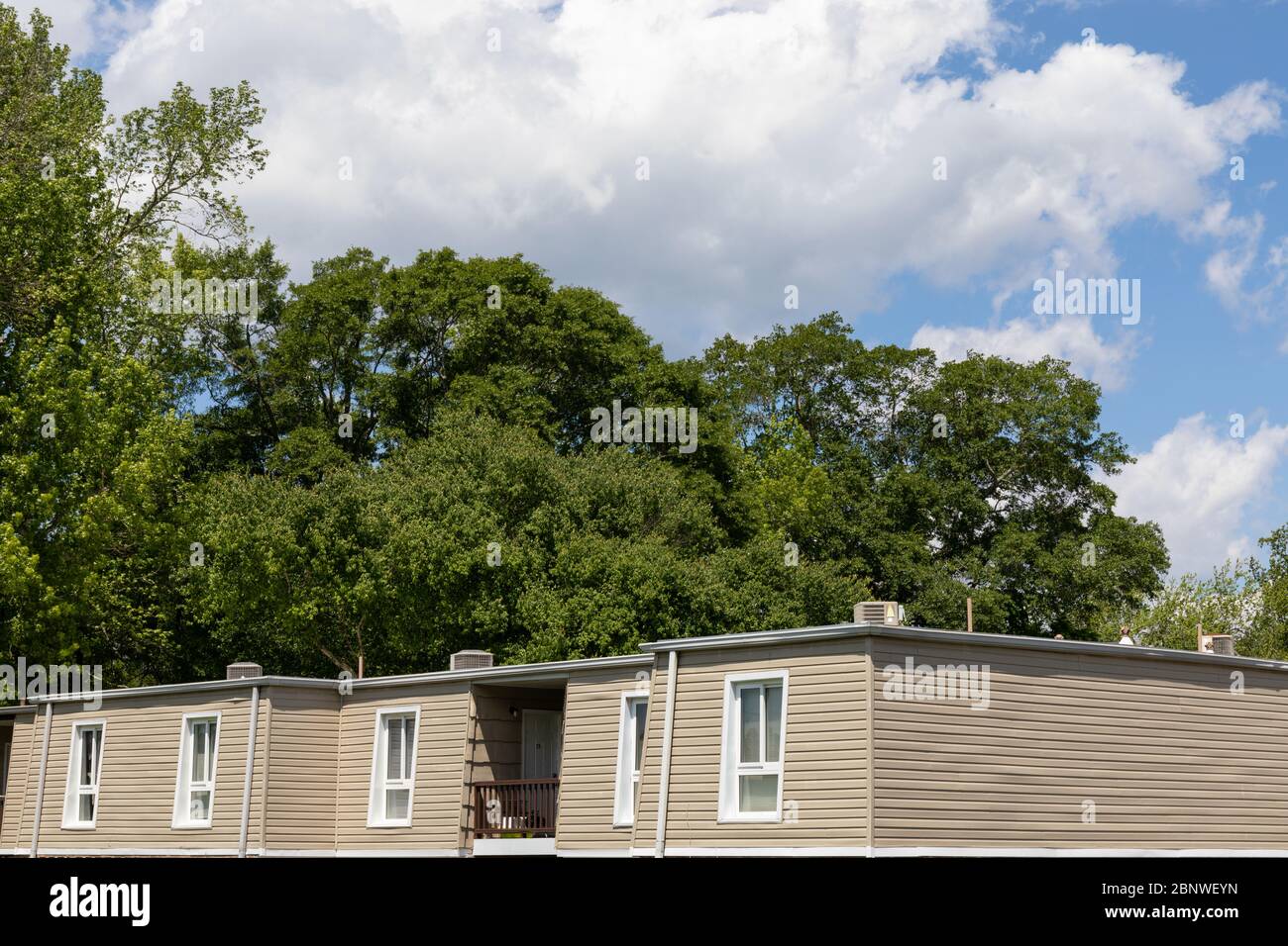 Generic apartment building upper level against trees with blue sky and ...