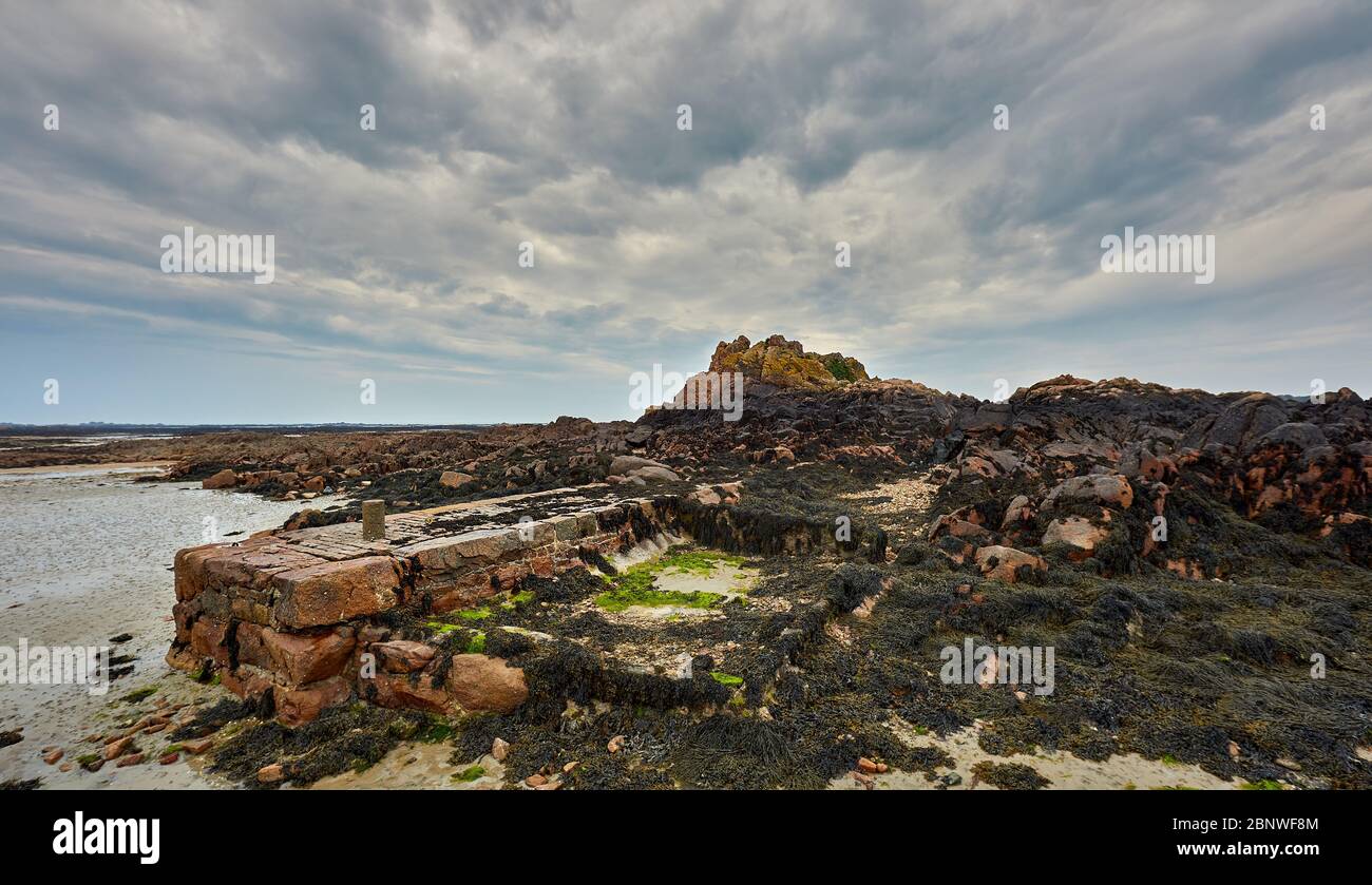 Imge of the beach at low tide with rocks, seaweed, small stone pier and ...