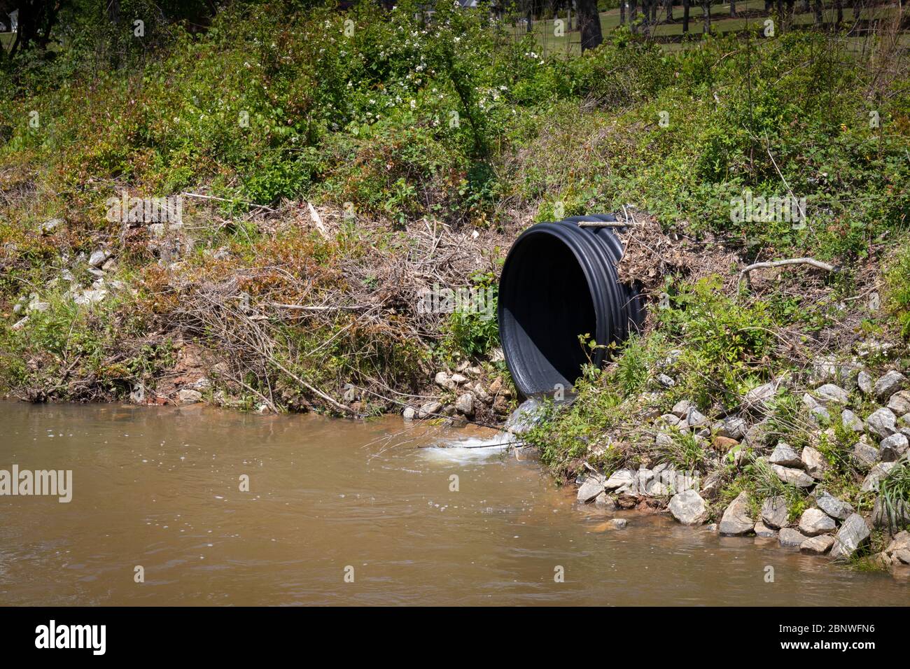 Black plastic drainage culvert pipe releasing water into a stream ...