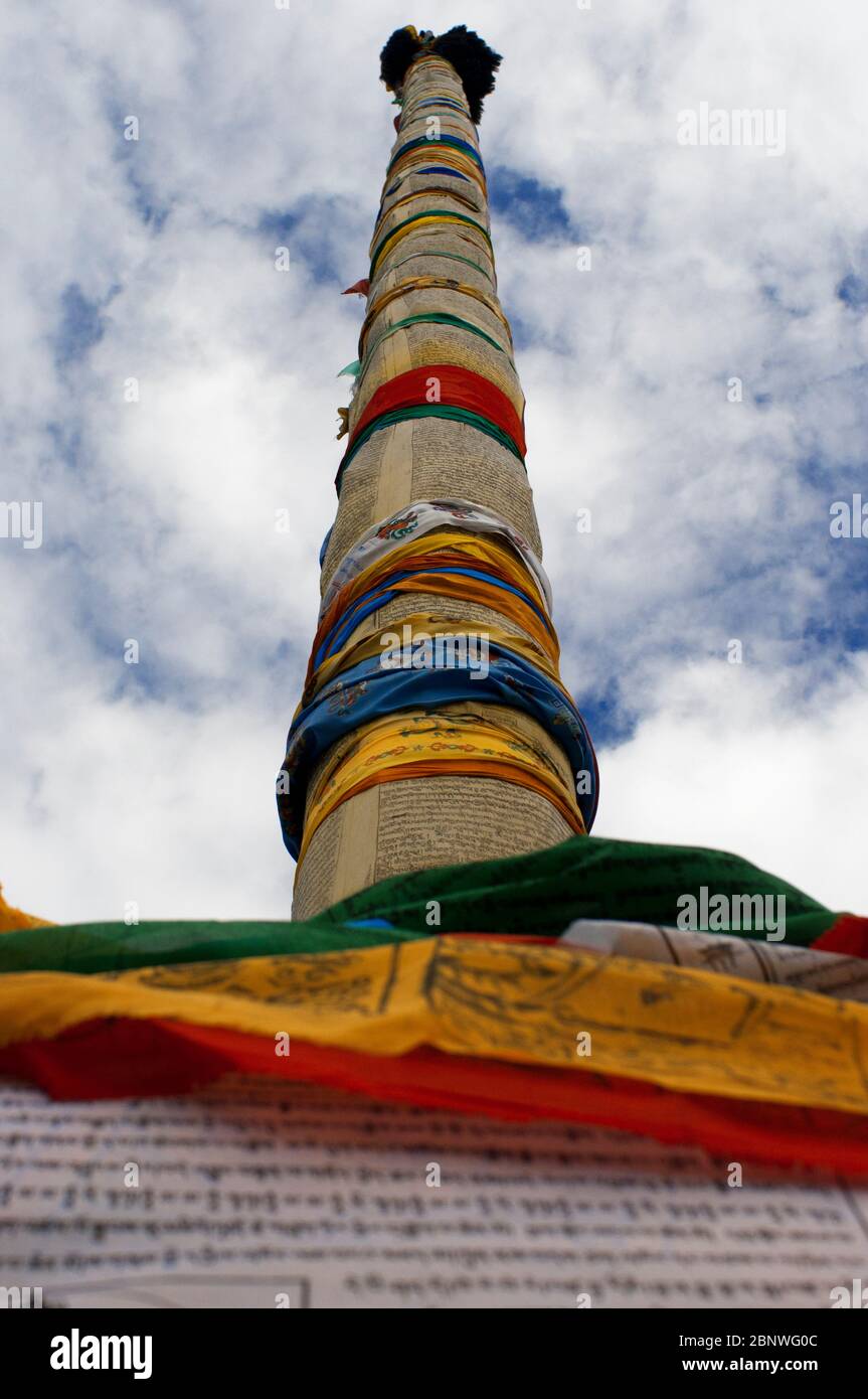 Tibetan Buddhist pilgrims walk around a holy pole decorated with prayer ...