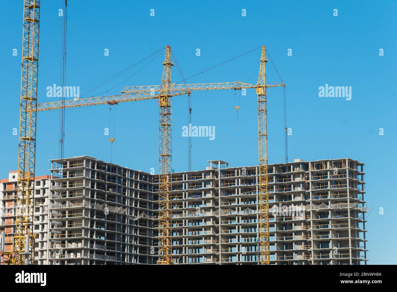 Two construction cranes near the unfinished buildings. Construction and ...