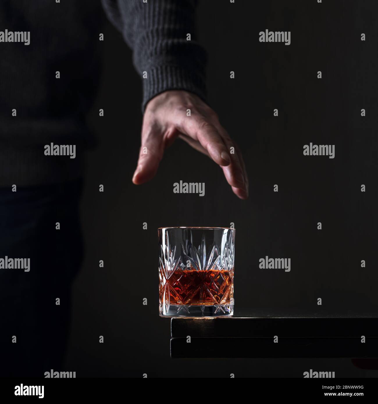 Man's hand reaches for a glass of alcohol. Conceptual image on the ...