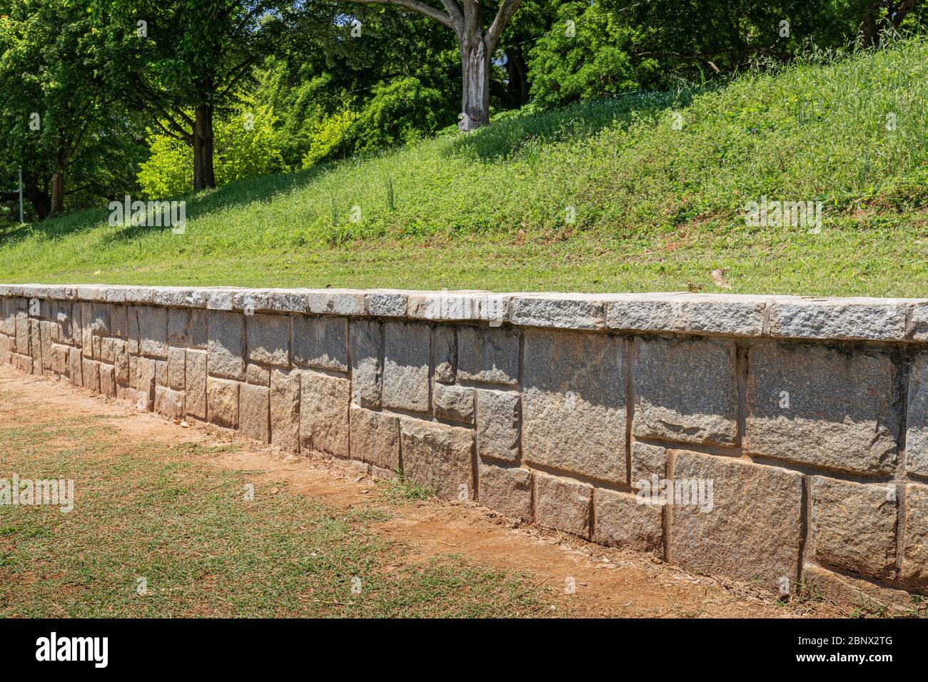 Stone retaining wall in a public park, green hills with ground cover ...