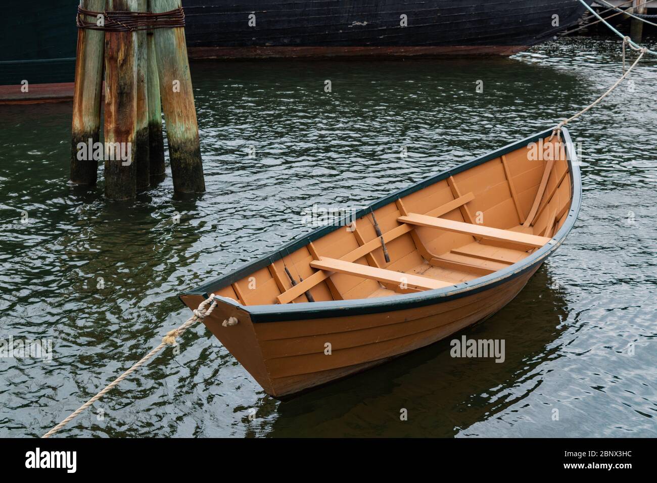 Small rowboat tied up beside a larger sailing vessel and dolphin pier ...