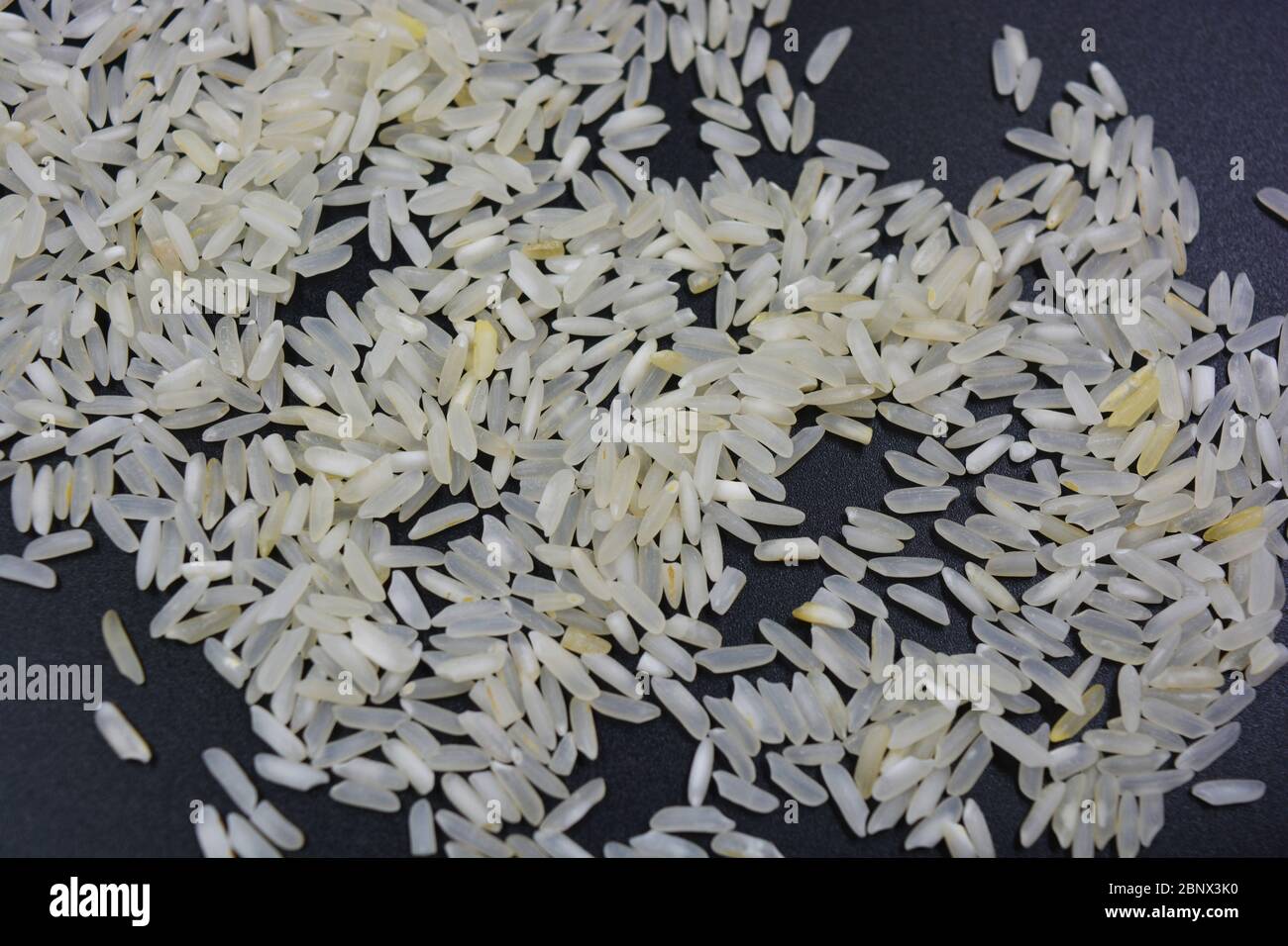 White steamed long-grain rice scattered on a black surface. Healthy and ...