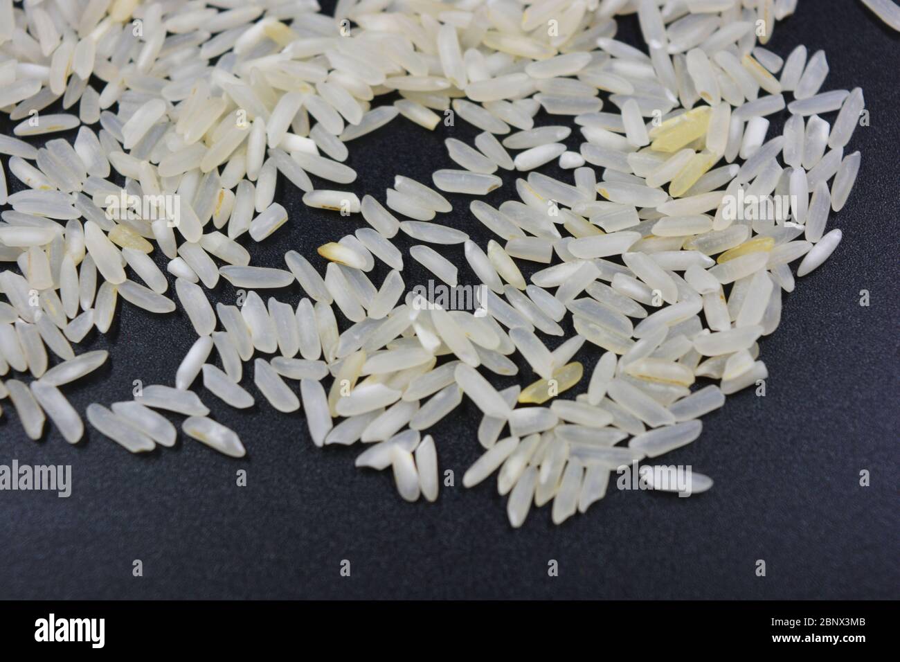 White steamed long-grain rice scattered on a black surface. Healthy and ...