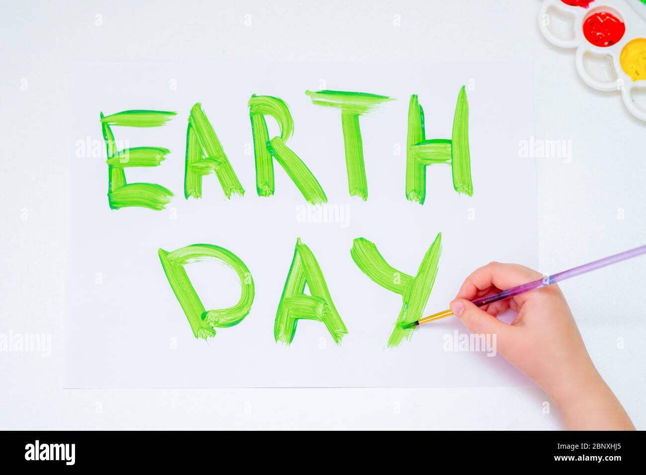 Child's hand writing words Earth Day by green watercolor on white sheet ...