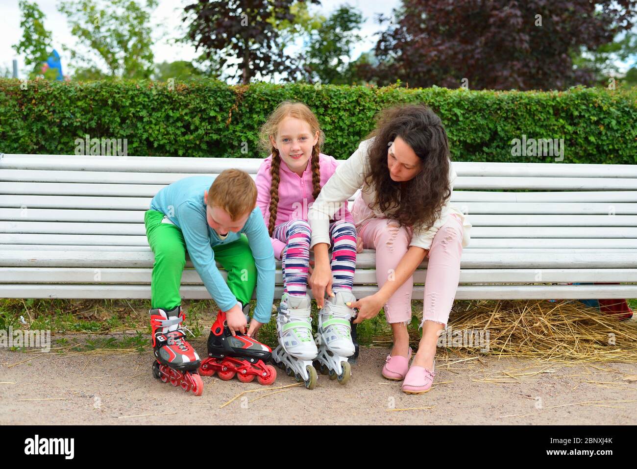 A Woman Sitting On A Bench And Helps Her Children To Fasten The Stock a-woman-sitting-on-a-bench-and-helps-her-children-to-fasten-the-stock