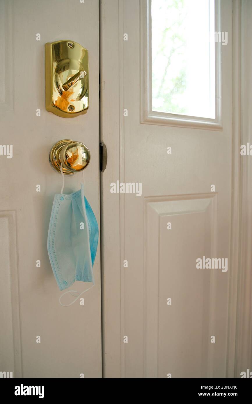 Face mask hanging from door handle on white door with sunlight coming ...