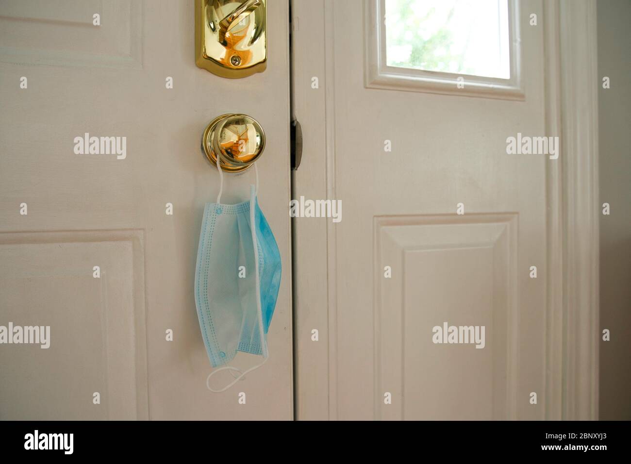 Face mask hanging from door handle on white door with sunlight coming ...