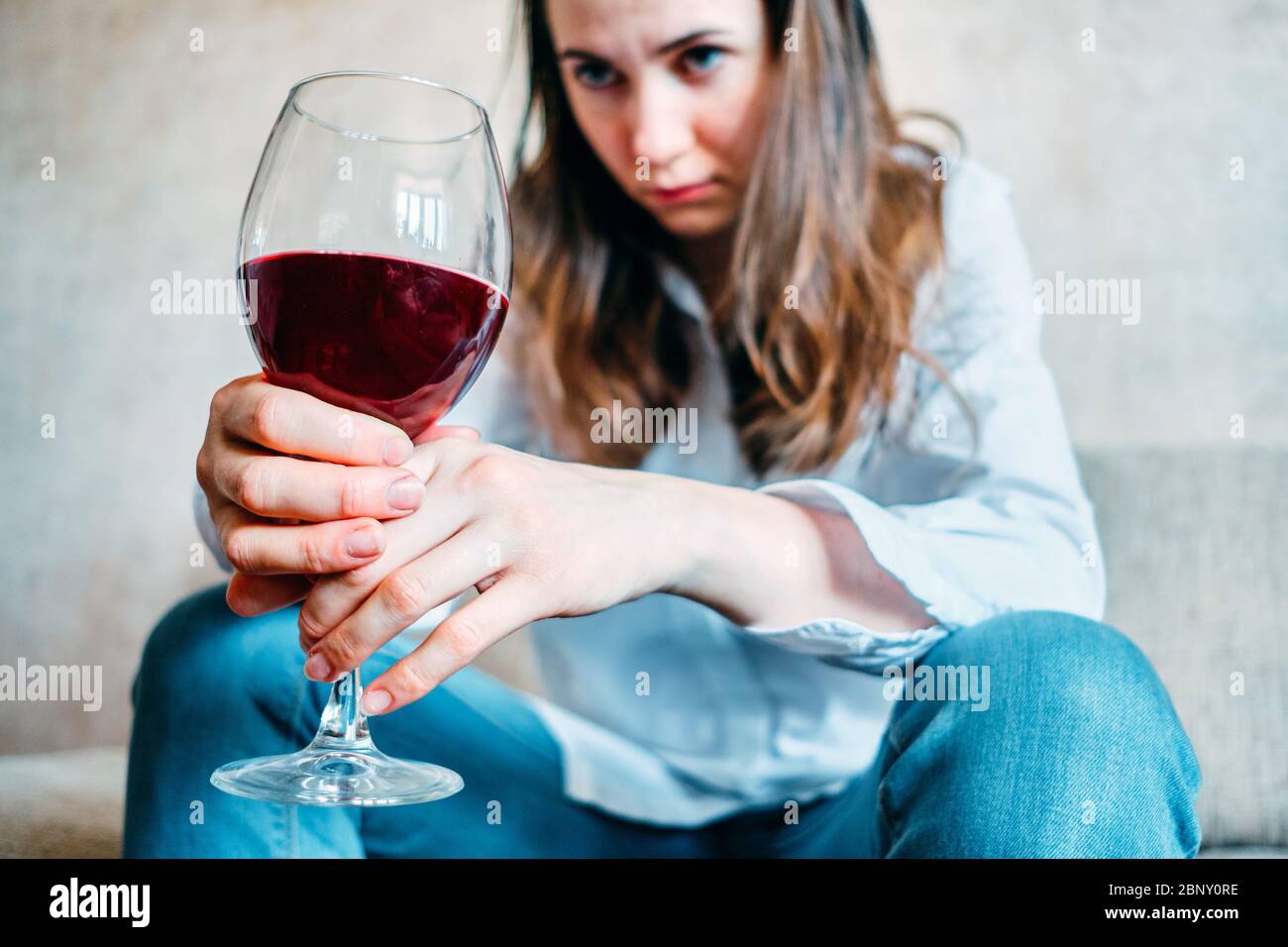 A drunk girl drinks wine and looks at a glass while sitting on a sofa ...