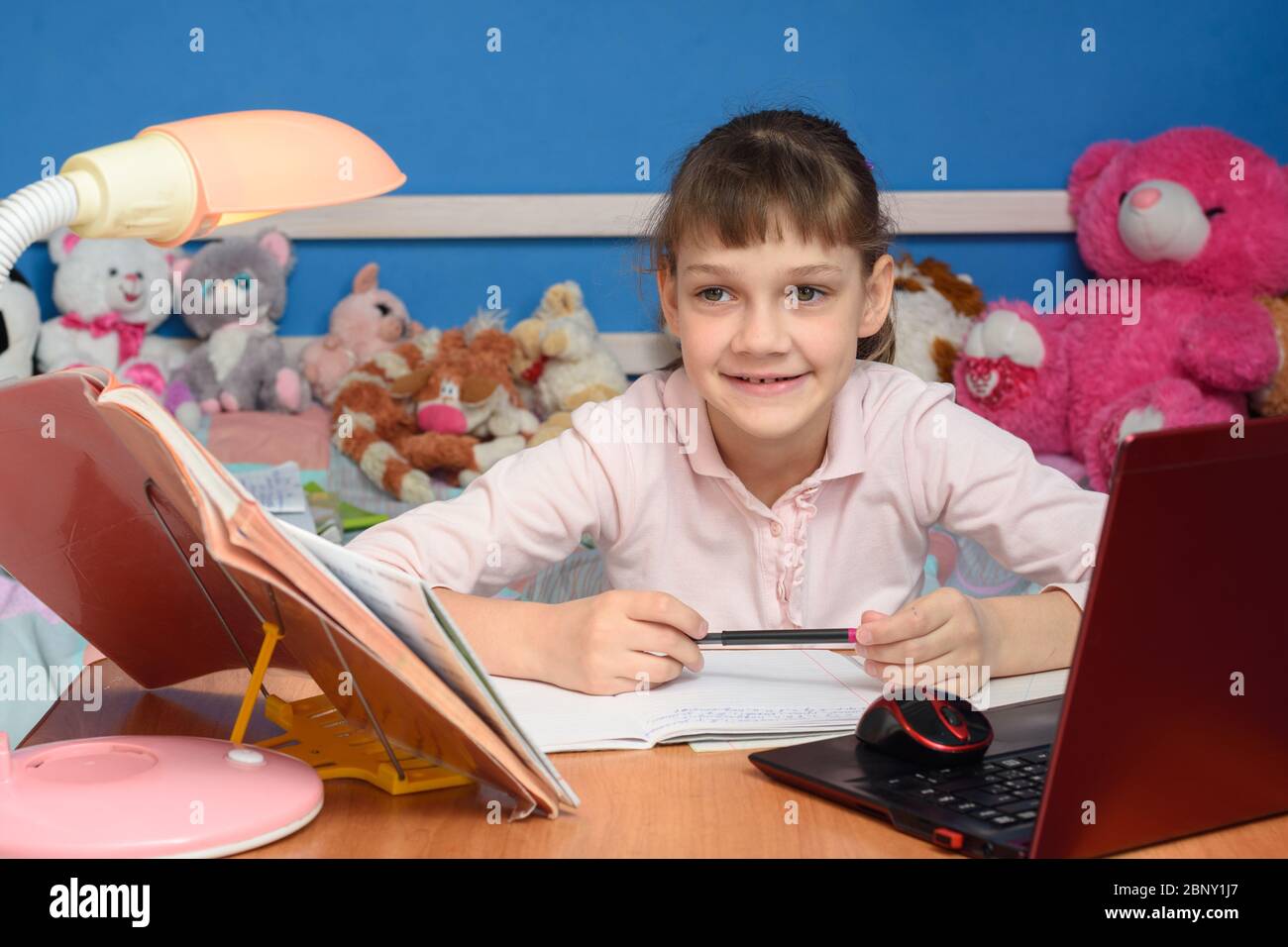 The girl in the children's room sits at the desk with a smile and does ...