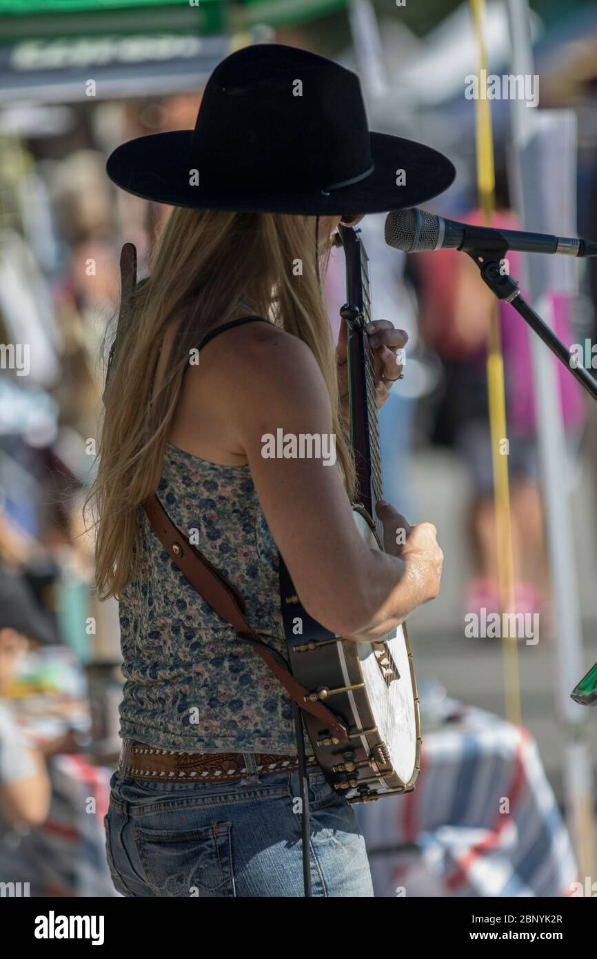 Pretty, blonde, female folk singer, playing banjoand singing at outdoor ...