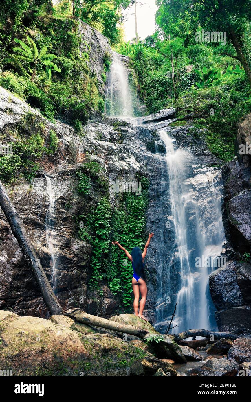 Young happy girl enjoing the waterfall. Woman standing in front of ...