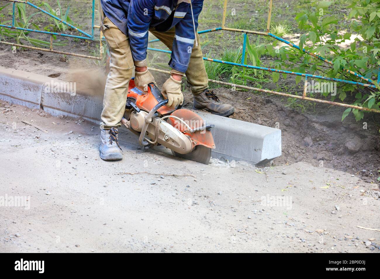 A worker using a portable cutter cuts asphalt along a concrete curb in ...