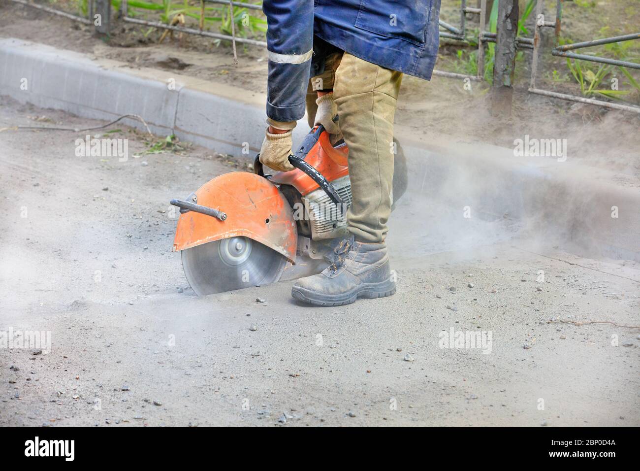 A worker using a portable petrol cutter and cutting a diamond blade ...