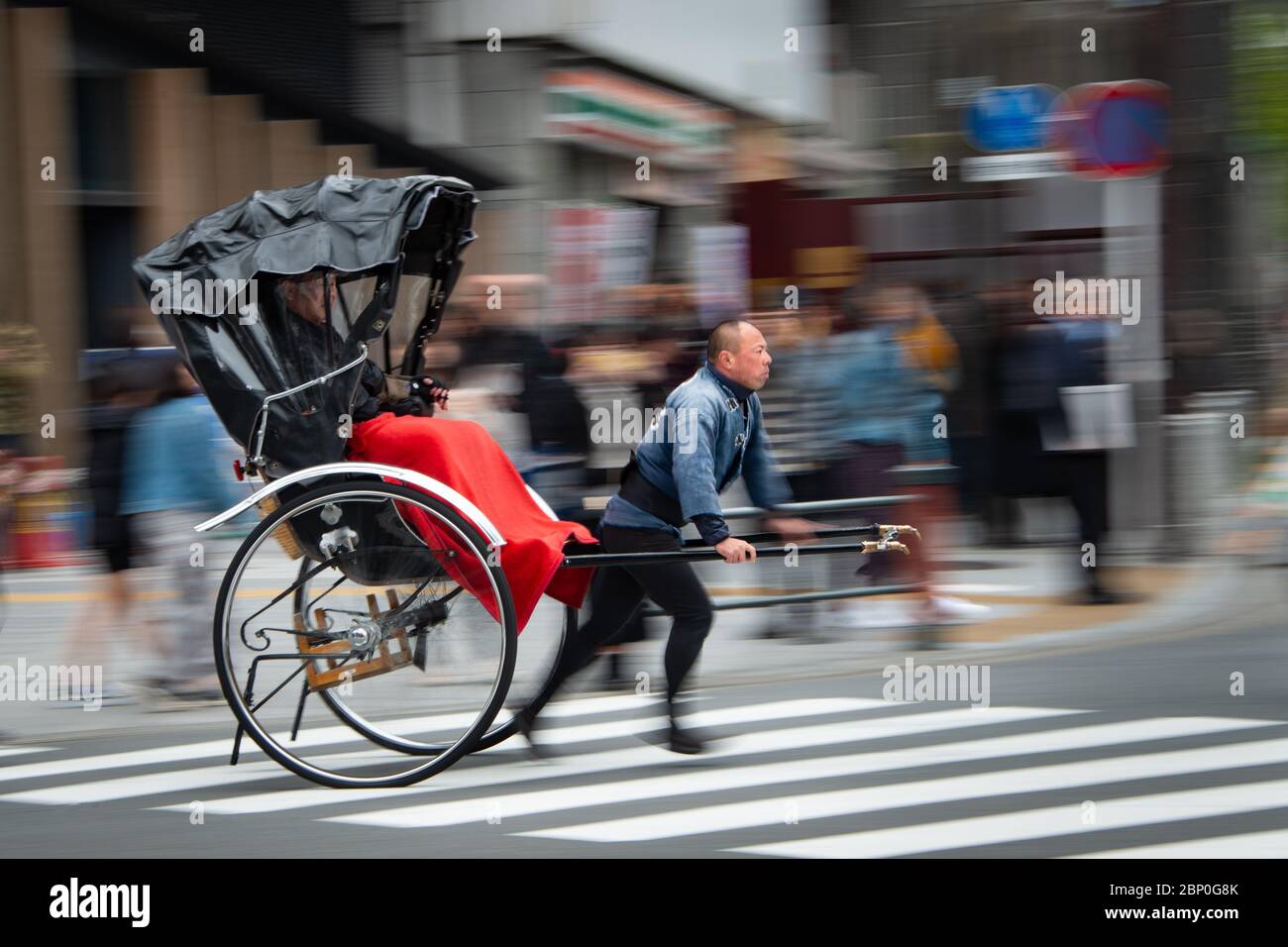 A rickshaw puller is pulling tourist in rickshaw on a busy Tokyo street ...