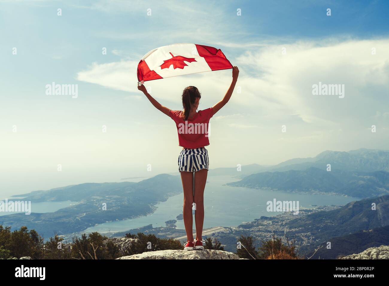 Child girl is waving Canadian flag on top of mountain at sky background ...