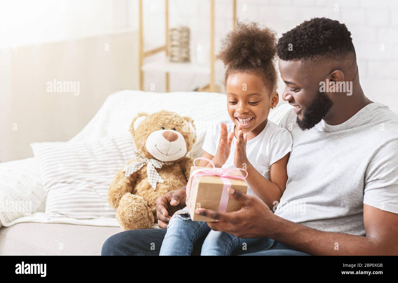 Excited black girl taking gift from daddy Stock Photo - Alamy