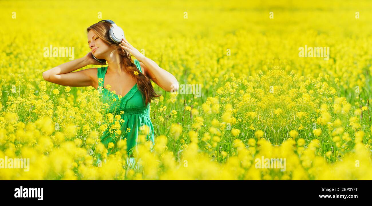 Young woman with headphones listening to music on oilseed flower field ...