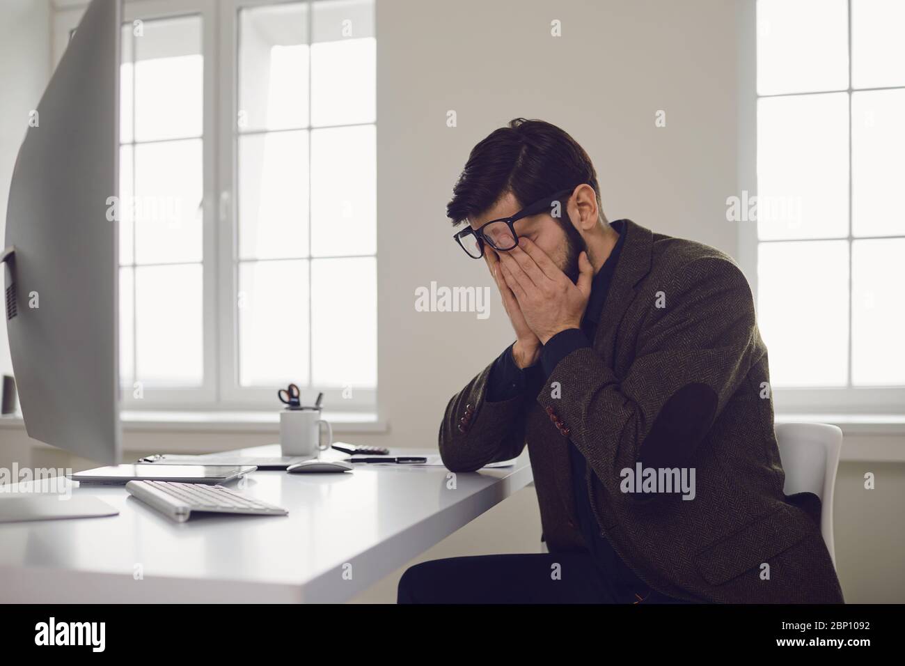 Exhausted tired worker at the workplace covered his face with his hands ...