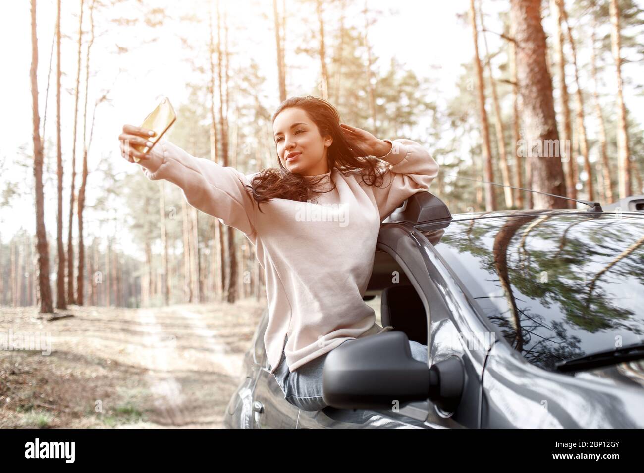 Happy young woman climbed out of a car window. Traveling by car in the ...