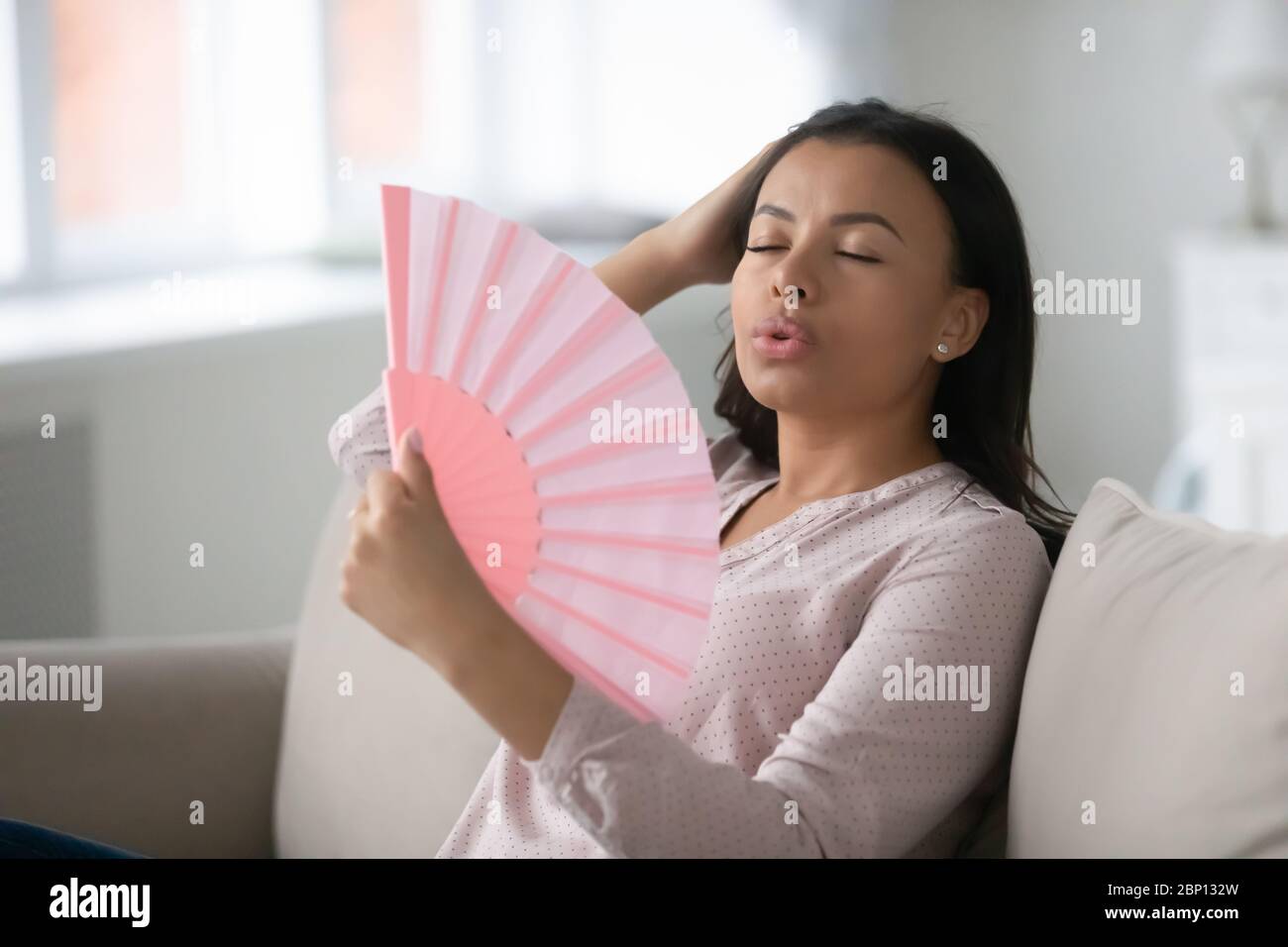 Overheated African woman escapes from heat with fan feels unwell Stock ...
