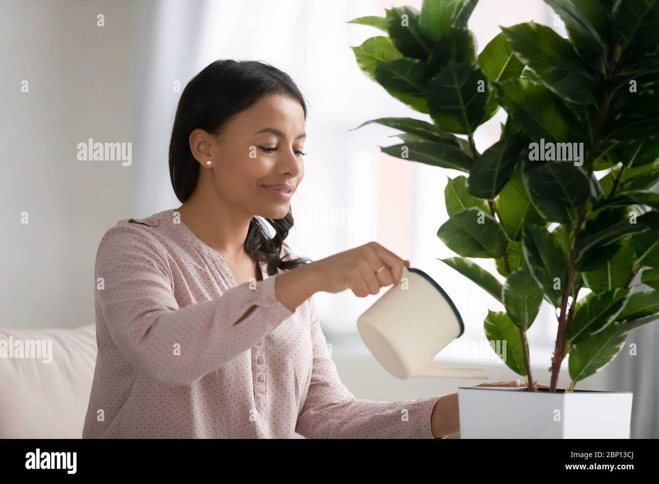 African young woman holding can watering houseplant Stock Photo - Alamy