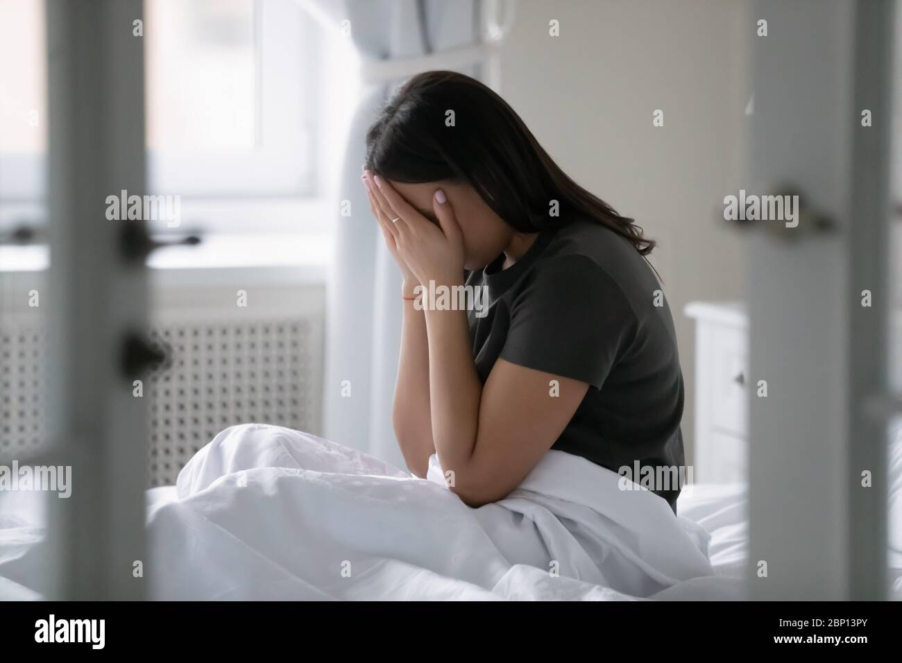 African young woman wake up seated in bed crying Stock Photo - Alamy