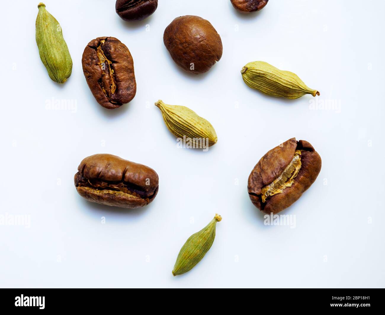 Flat lay. Coffee beans and cardamom grains are scattered on a white ...