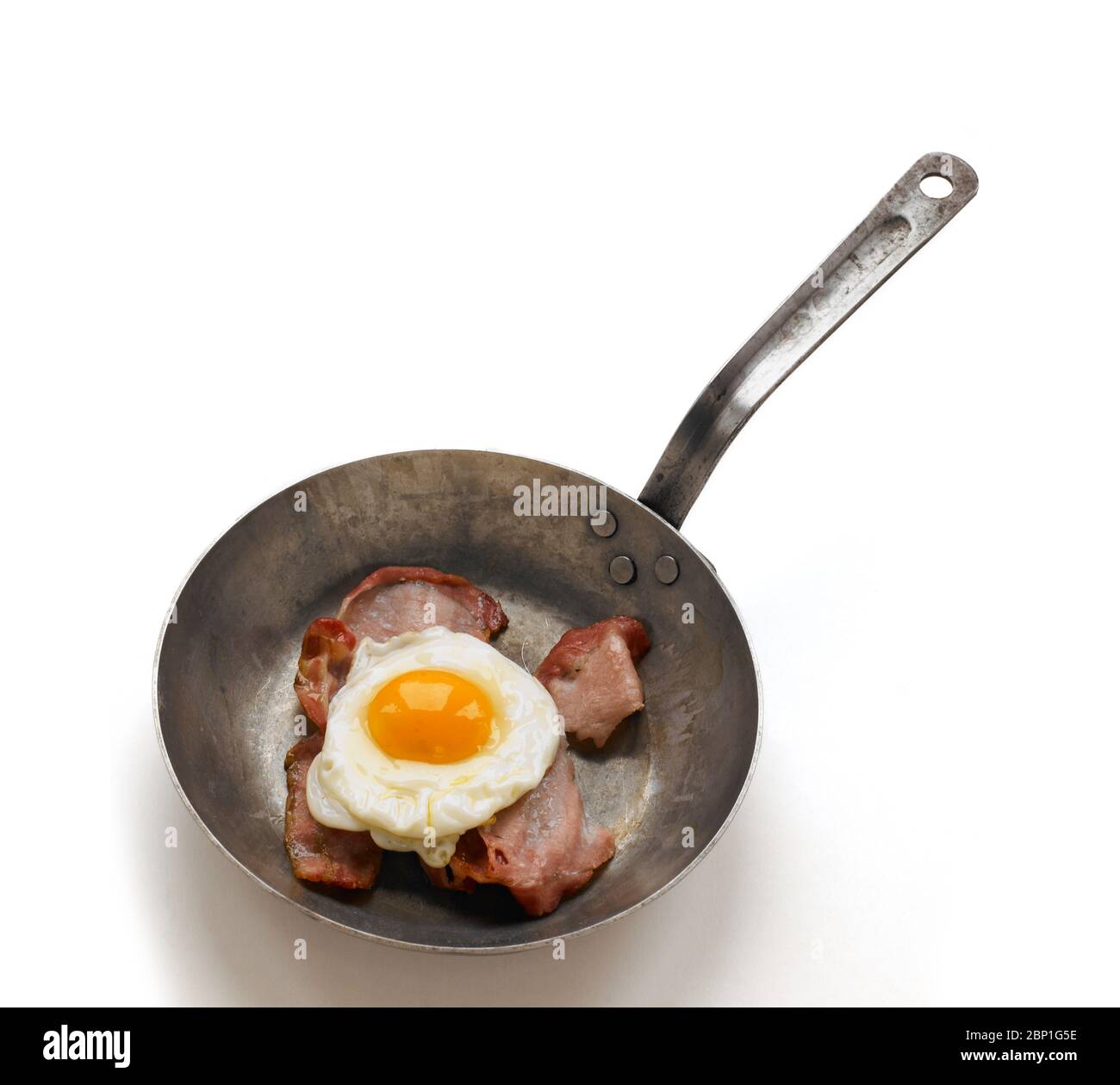 Cast iron frying pan with two bacon rashers and egg on white background ...