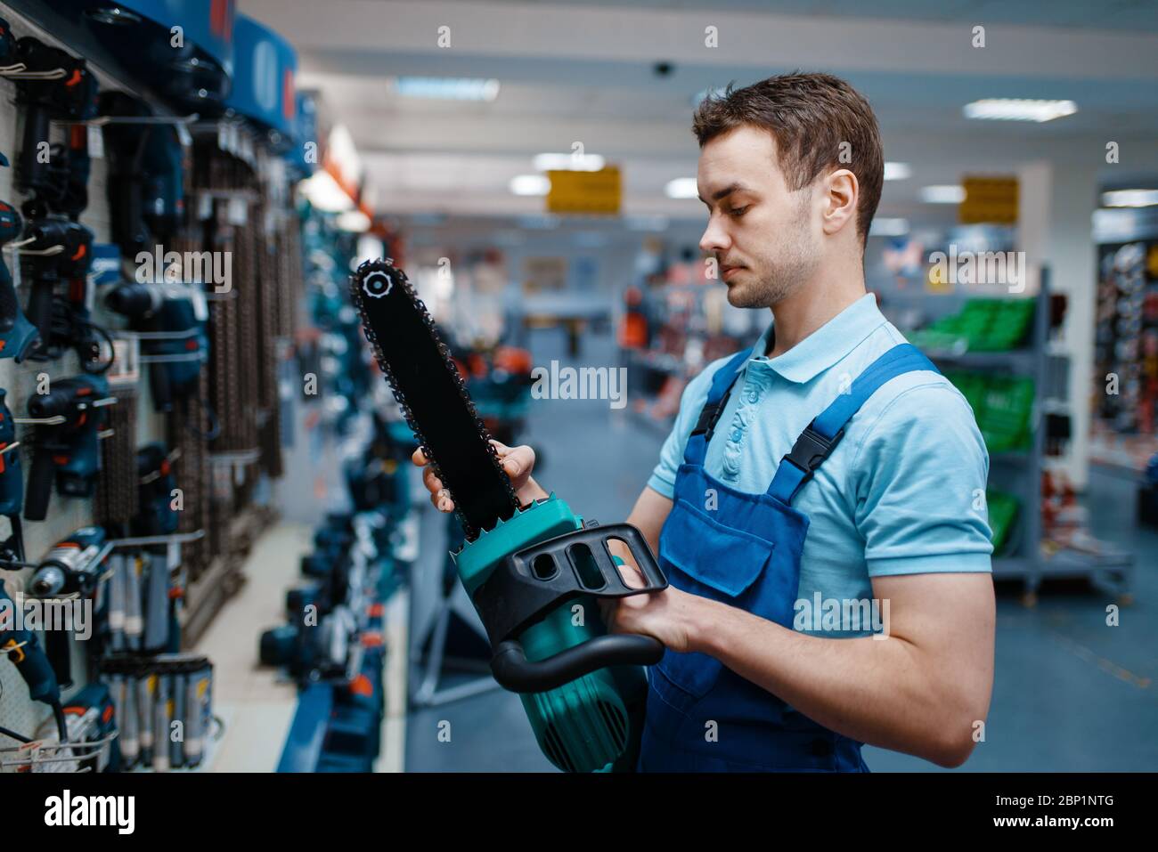 Worker in uniform holds electric saw in tool store Stock Photo - Alamy