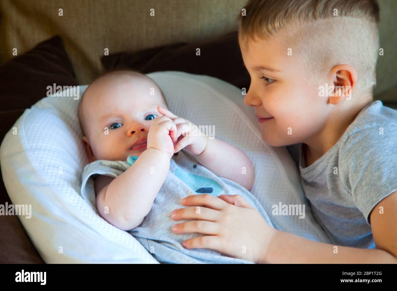 Two brothers older and younger on the couch. Newborn baby and boy of ...