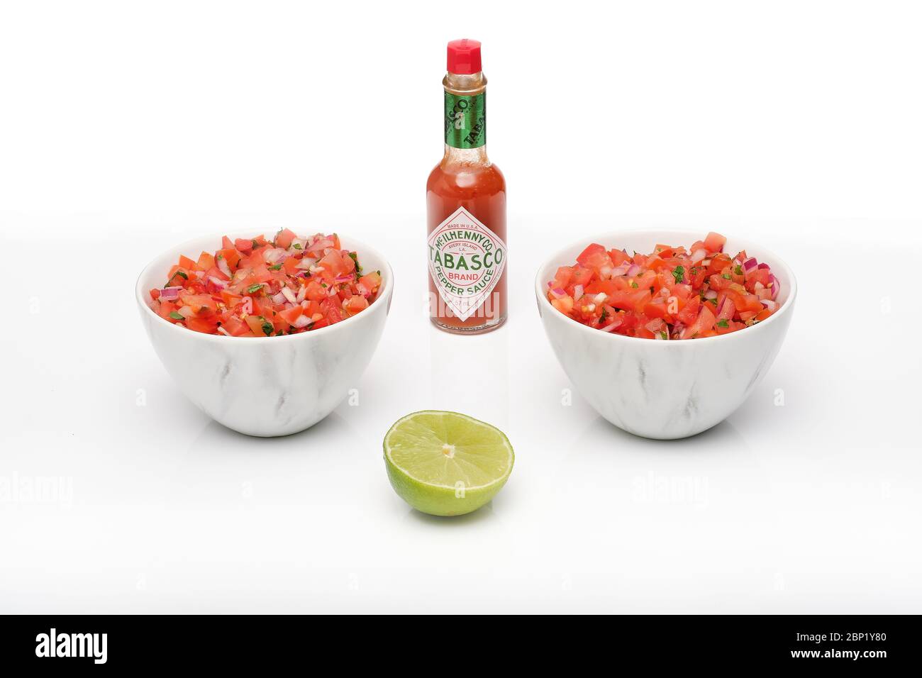2 identical bowls containing freshly made salsa with a bottle of ...