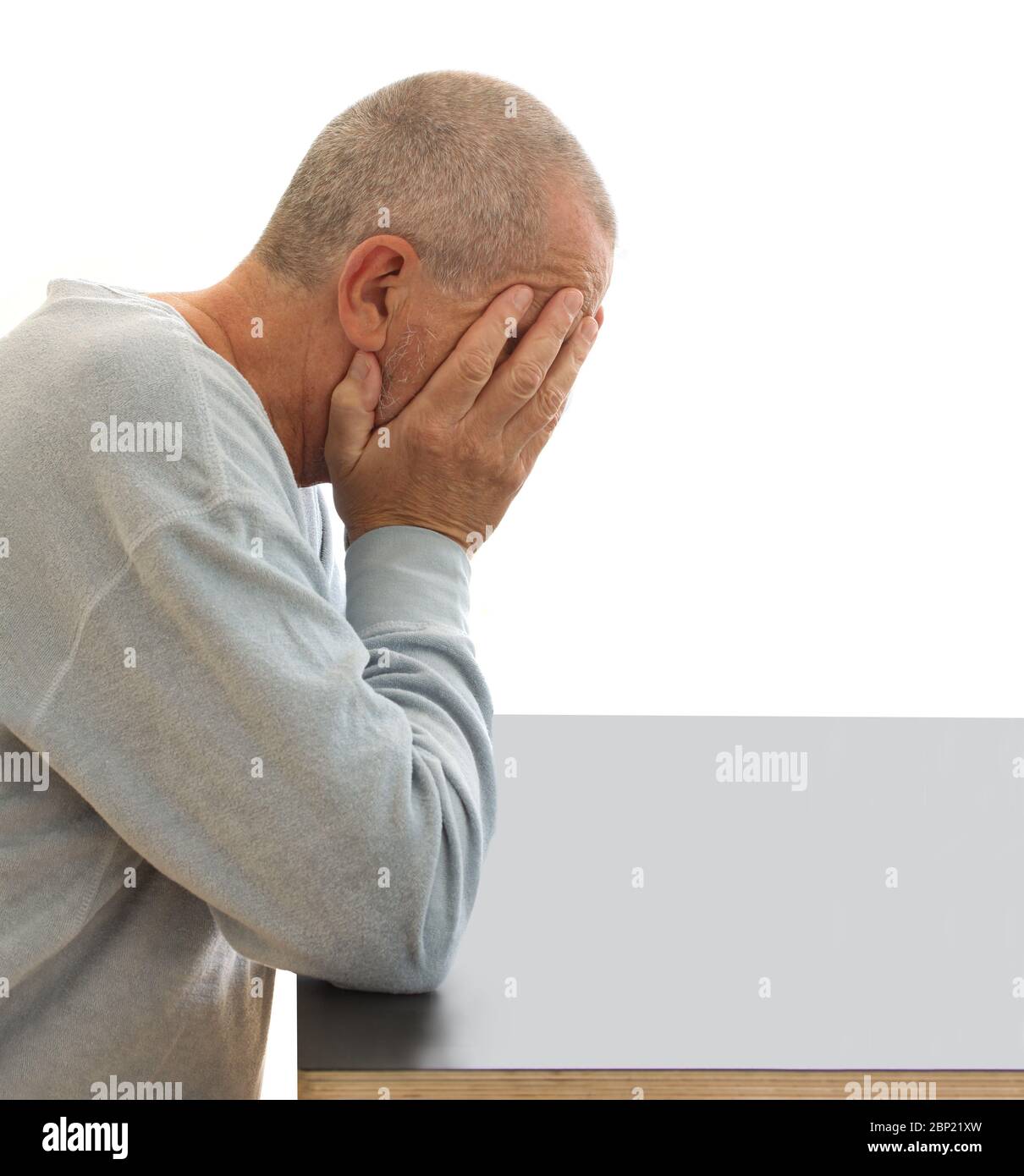 Ashamed and depressed man hiding his face with his hands by a table ...