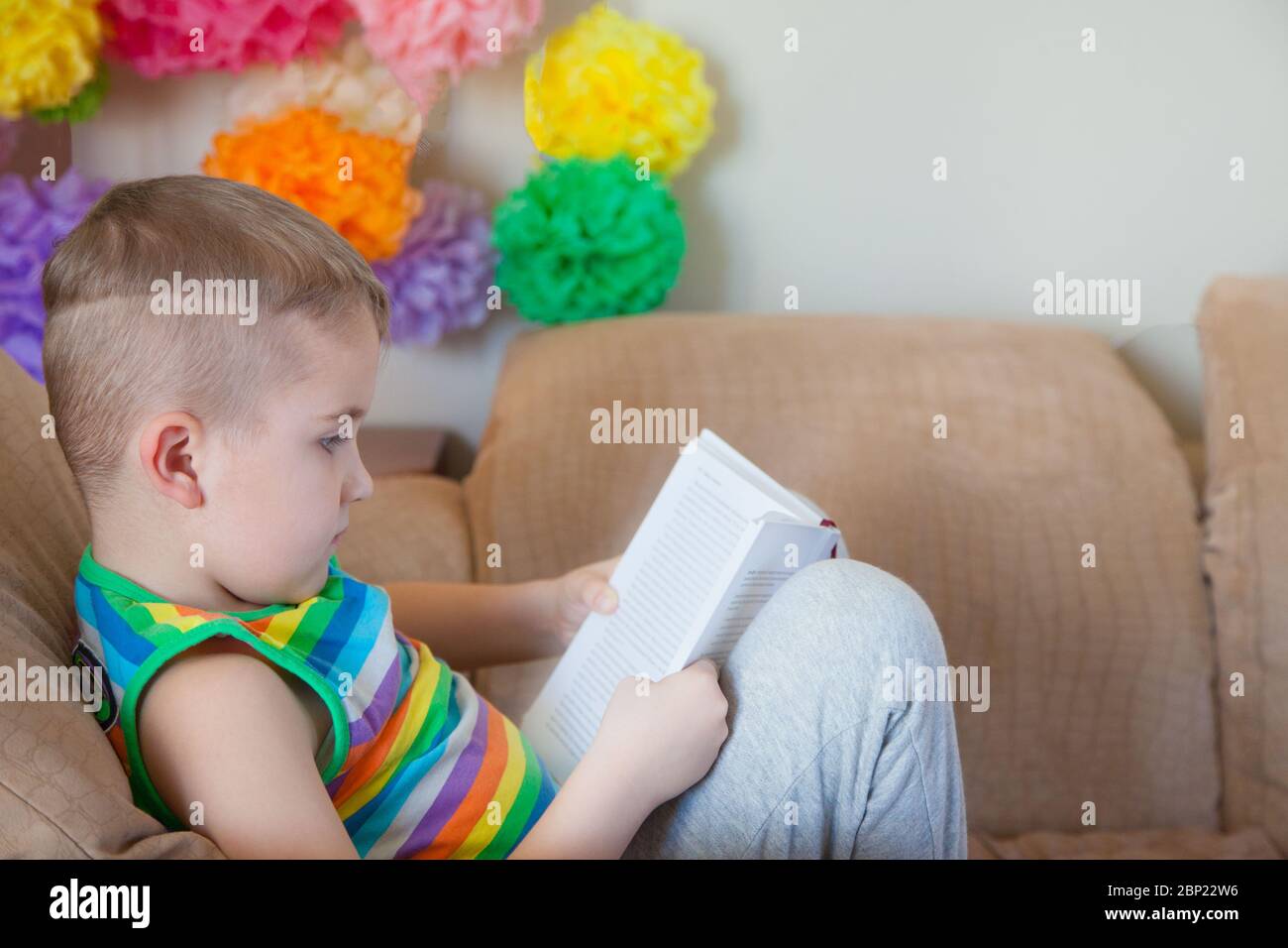 Young boy reading a book while sitting on the sofa Stock Photo - Alamy