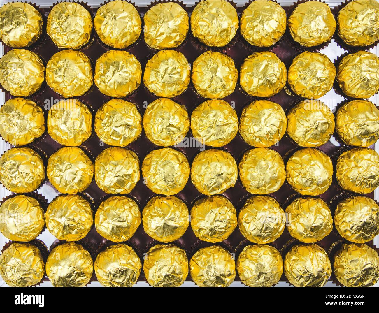 a lot of shiny golden chocolate wrapper in line on white background ...
