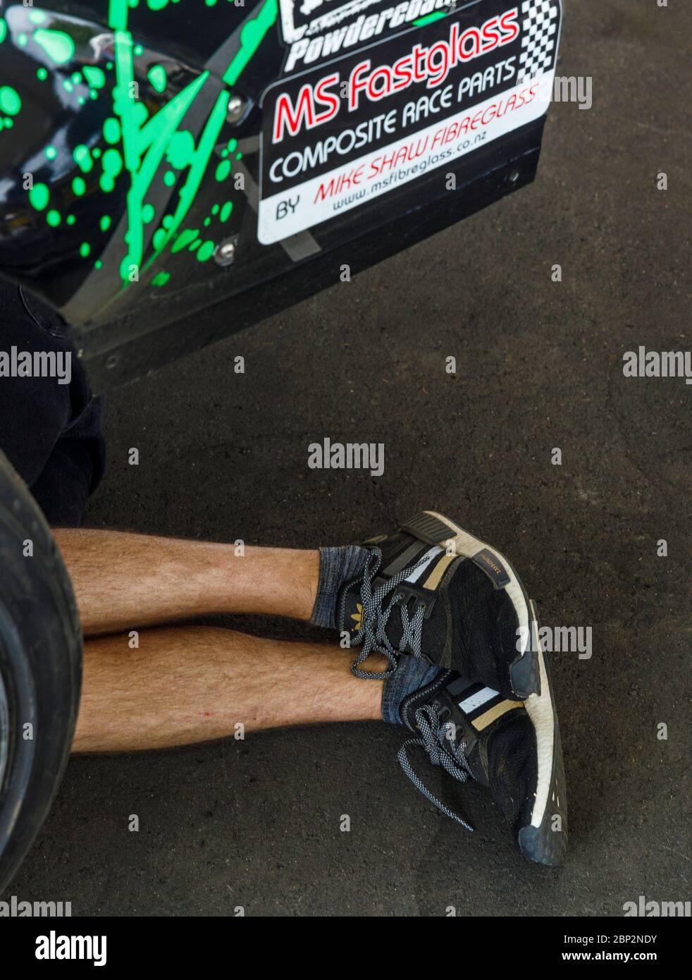 Mechanic's legs on the garage floor as he works underneath a race car ...