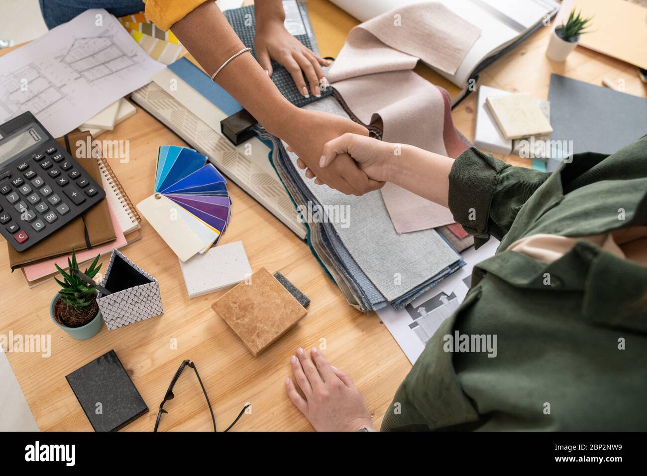 Young female designer of interior and her client shaking hands over ...