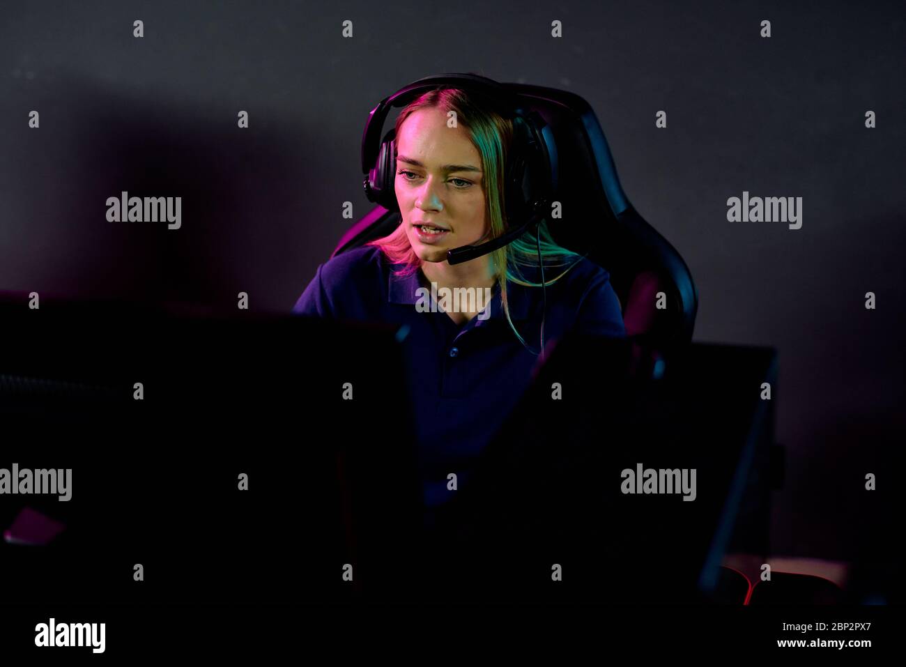 Young serious blond female e-sport gamer in headset looking at computer ...