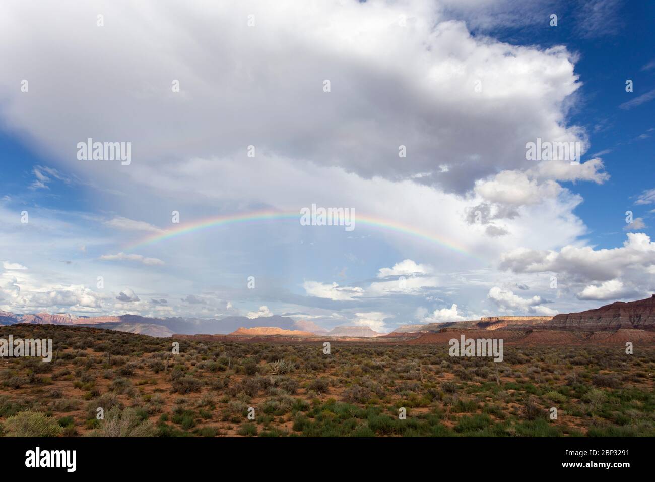 Rainbow under a thunderhead cloud set against the red landscape of ...