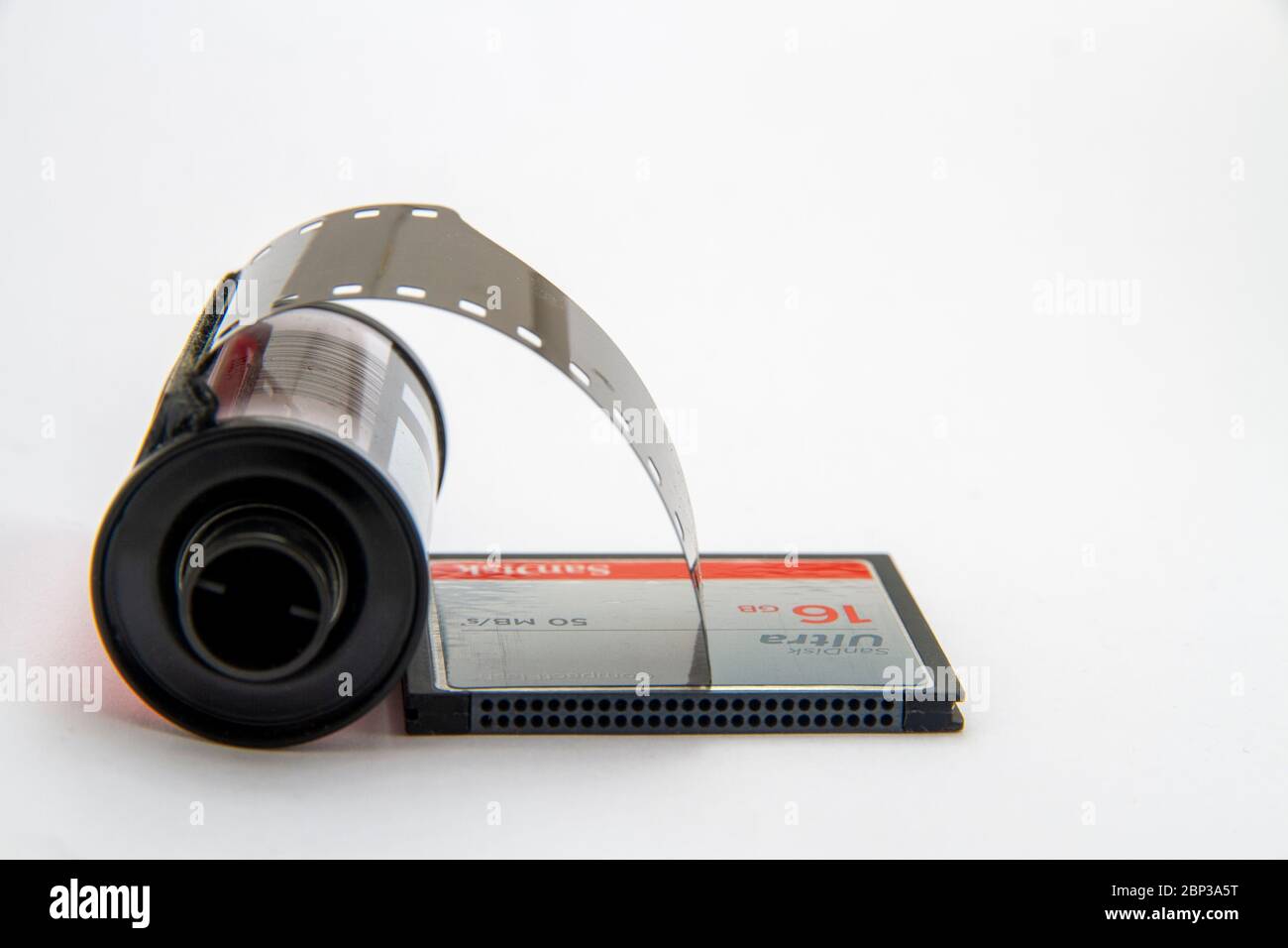 A 35mm film roll lies next to a 16GB sd card against a plain white ...