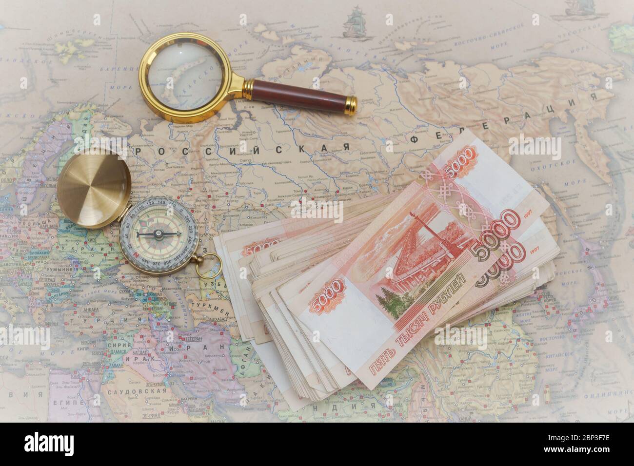 A compass with a bundle of big money and a magnifying glass are on the ...