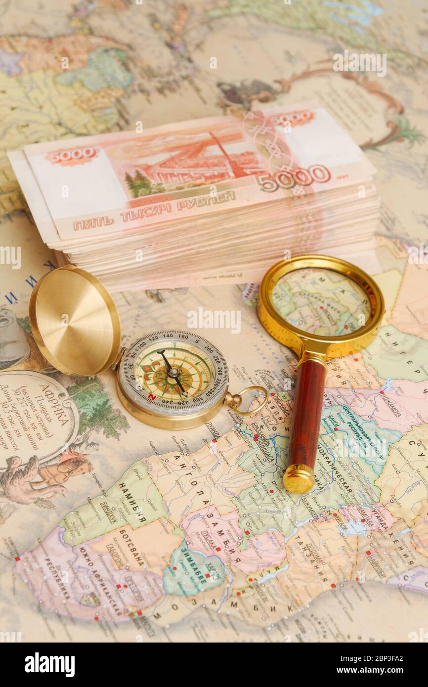 A compass with a bundle of big money and a magnifying glass are on the ...