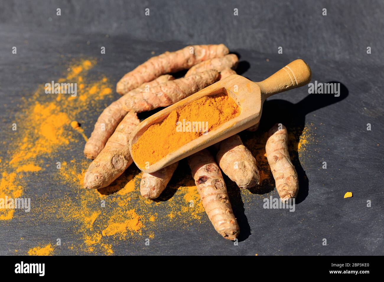 Turmeric powder (Kurkuma) in a wooden spoon and roots on a dark table ...